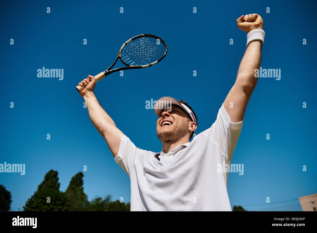 A joyful male tennis player raises his arms in triumph under a clear ...