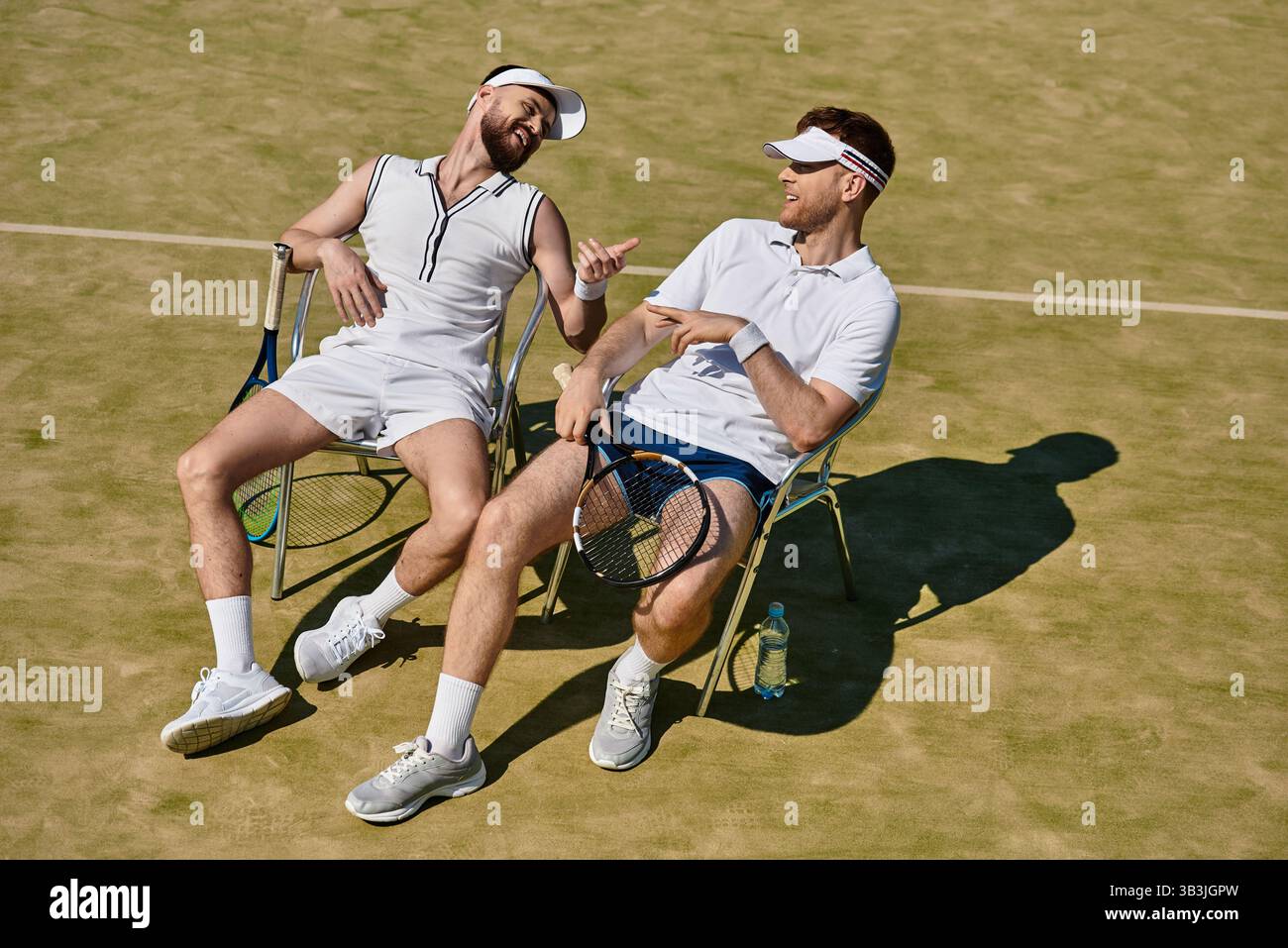 Two handsome men relax and laugh together on a summer tennis court ...