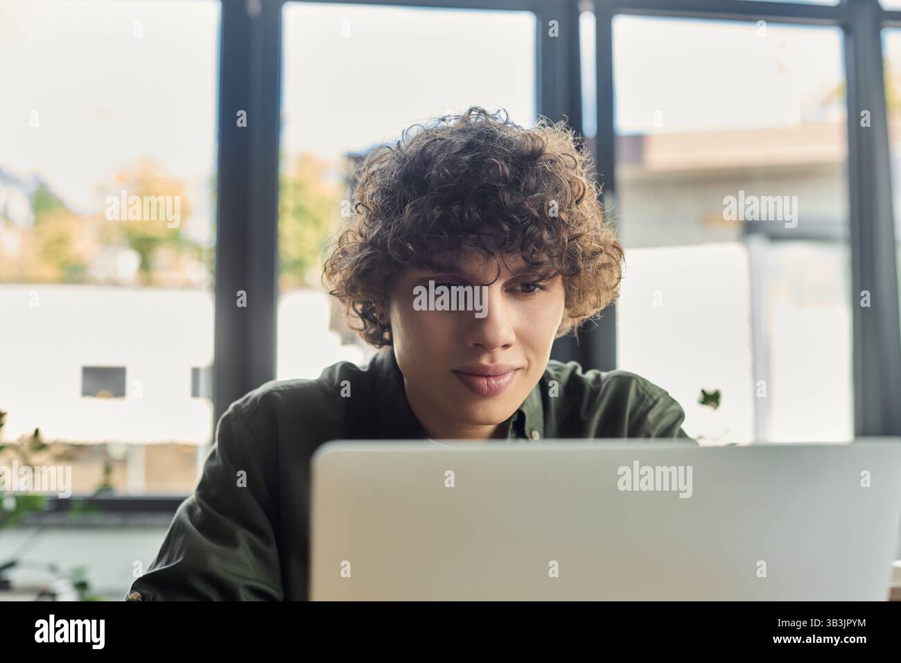 A focused person works on a laptop in a bright, plant filled office ...