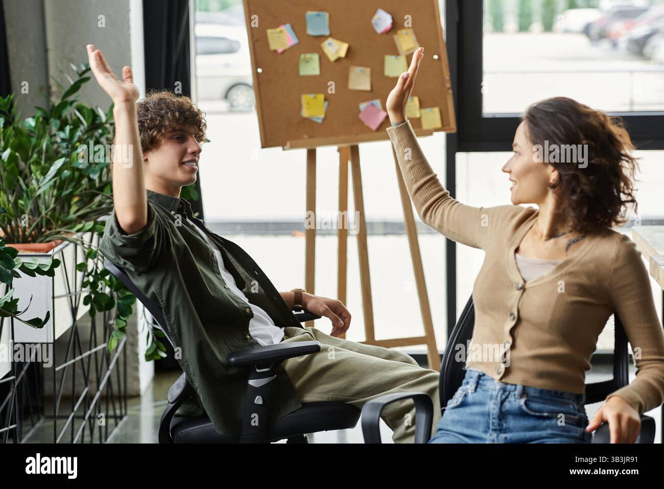 Two colleagues excitedly brainstorm together in a modern workspace ...