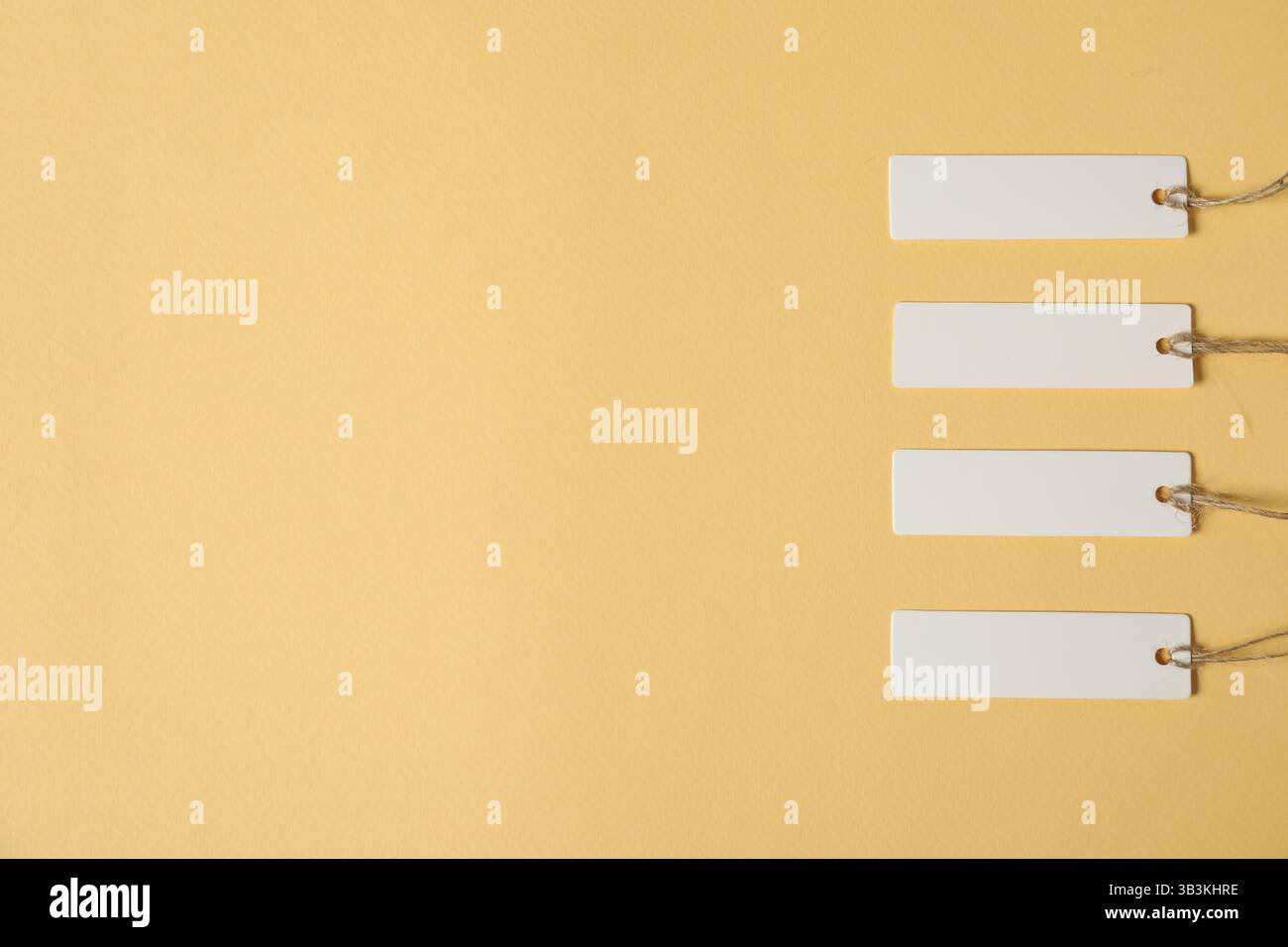 Blank tags with strings on pale yellow background, flat lay. Space for ...
