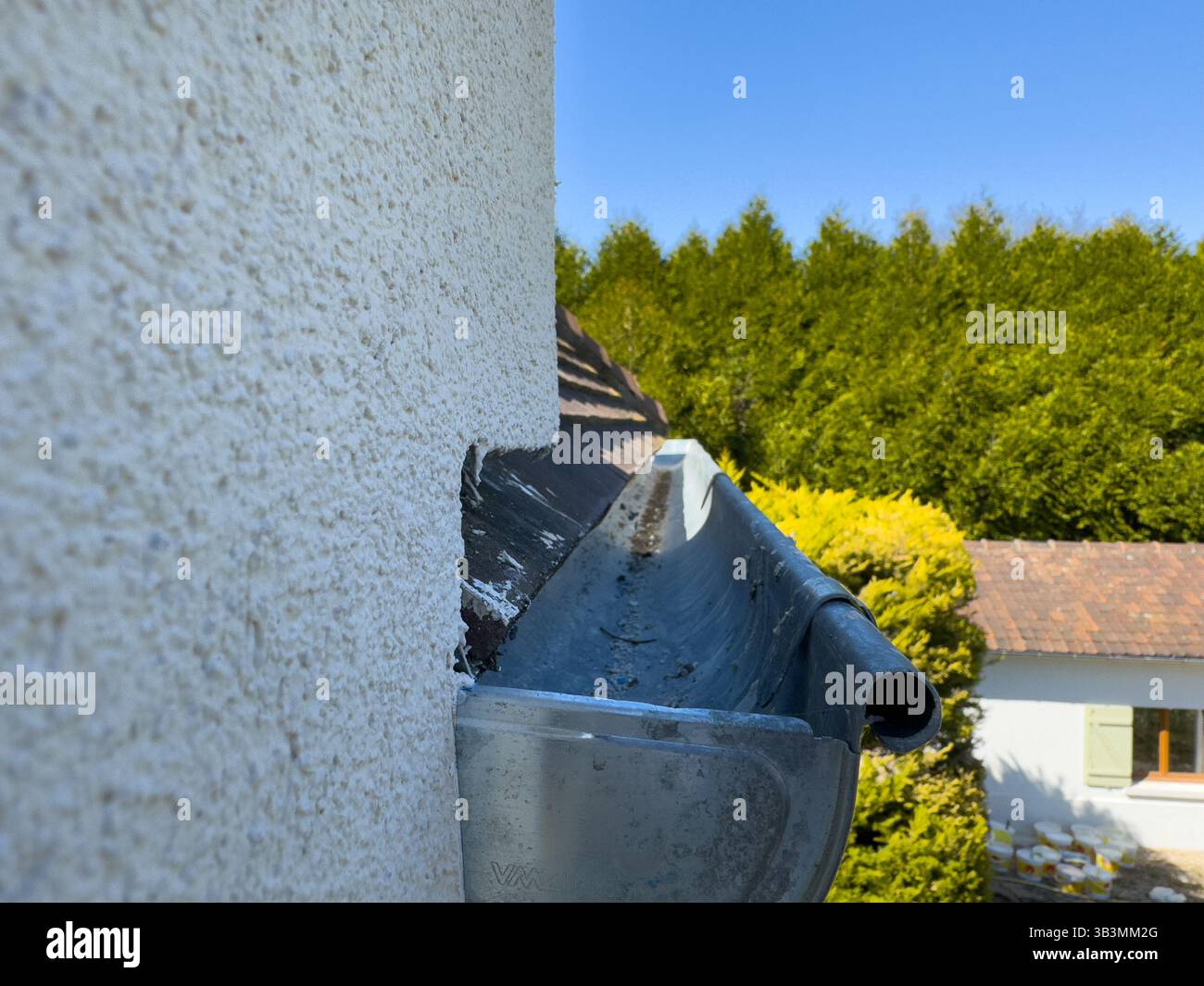 Gutter system on a sunny day with lush greenery and house in the ...