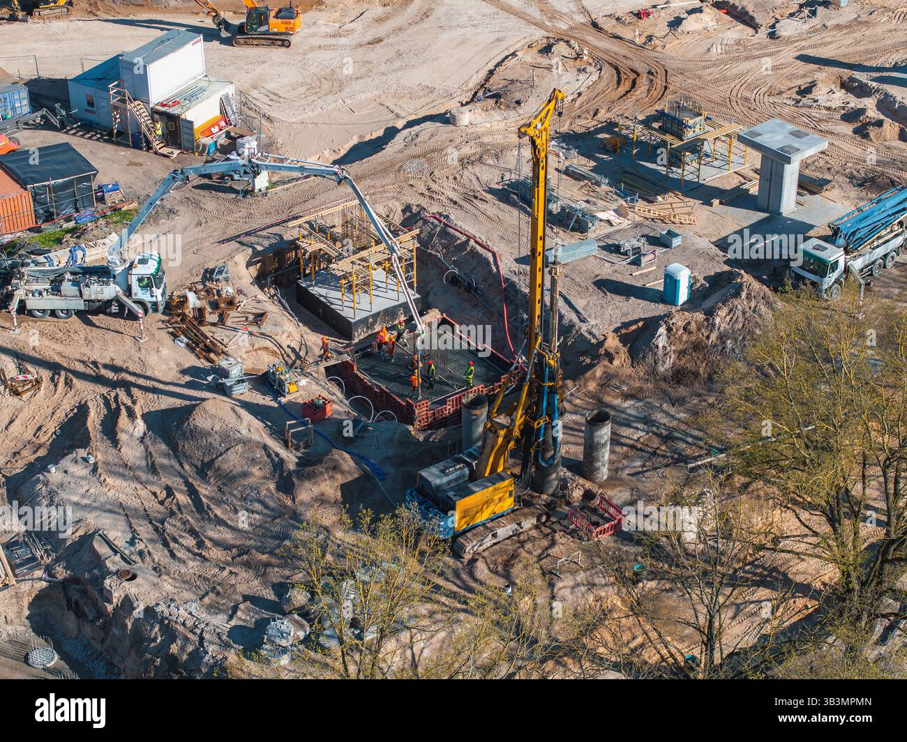 Active construction site with a yellow drilling rig, workers, machinery ...