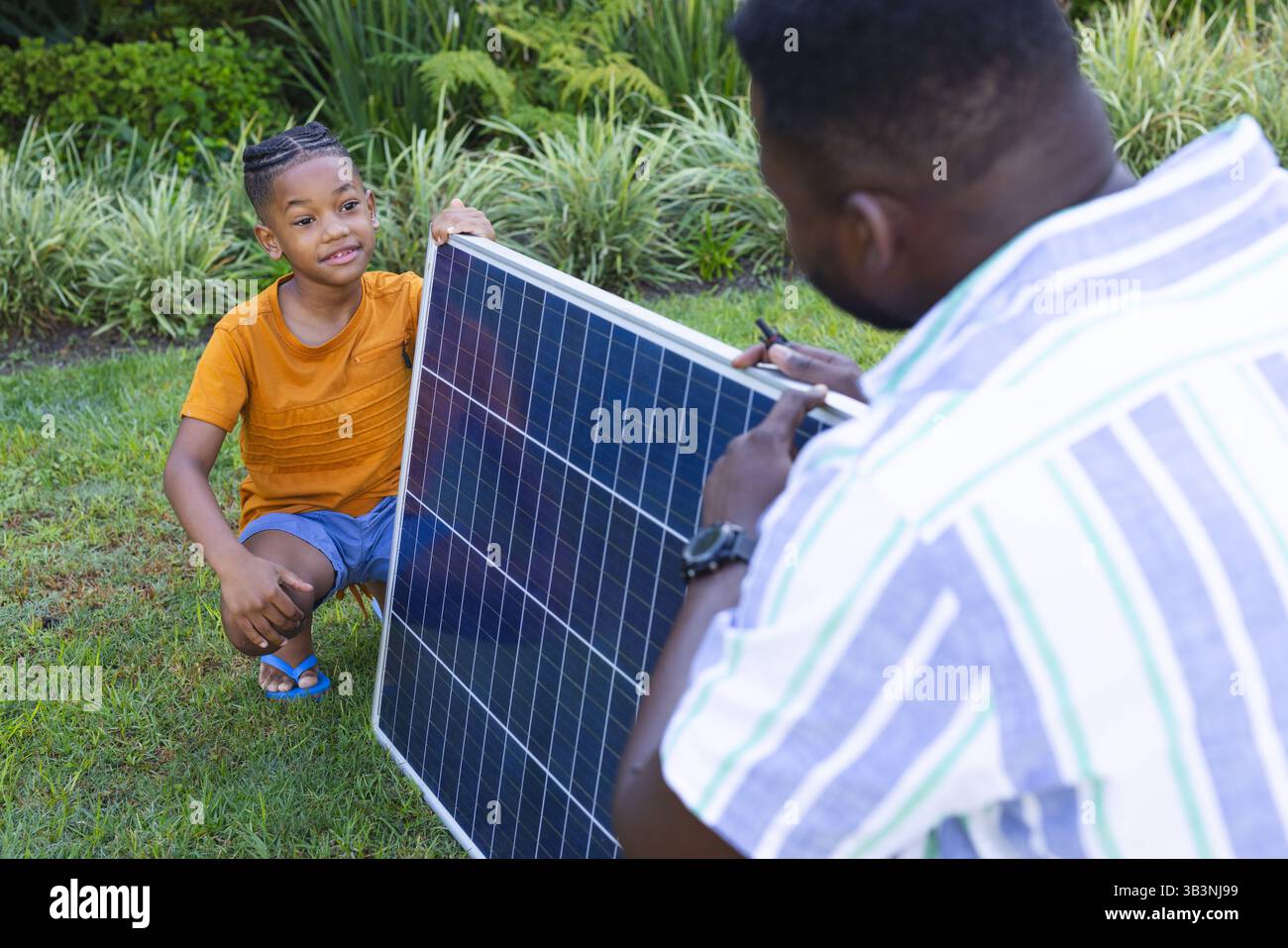 Kneeling diverse father and son installing solar panel on lawn in ...