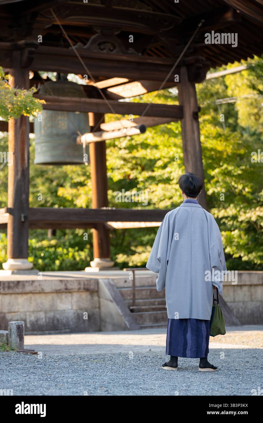 Man in traditional Kimono standing beside a large bronze temple bell at ...
