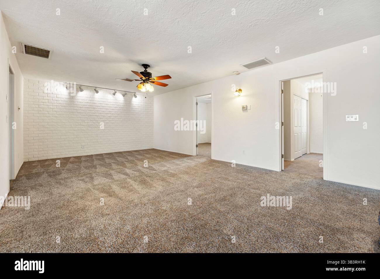 An empty living room featuring a ceiling fan and carpeting on the floor ...
