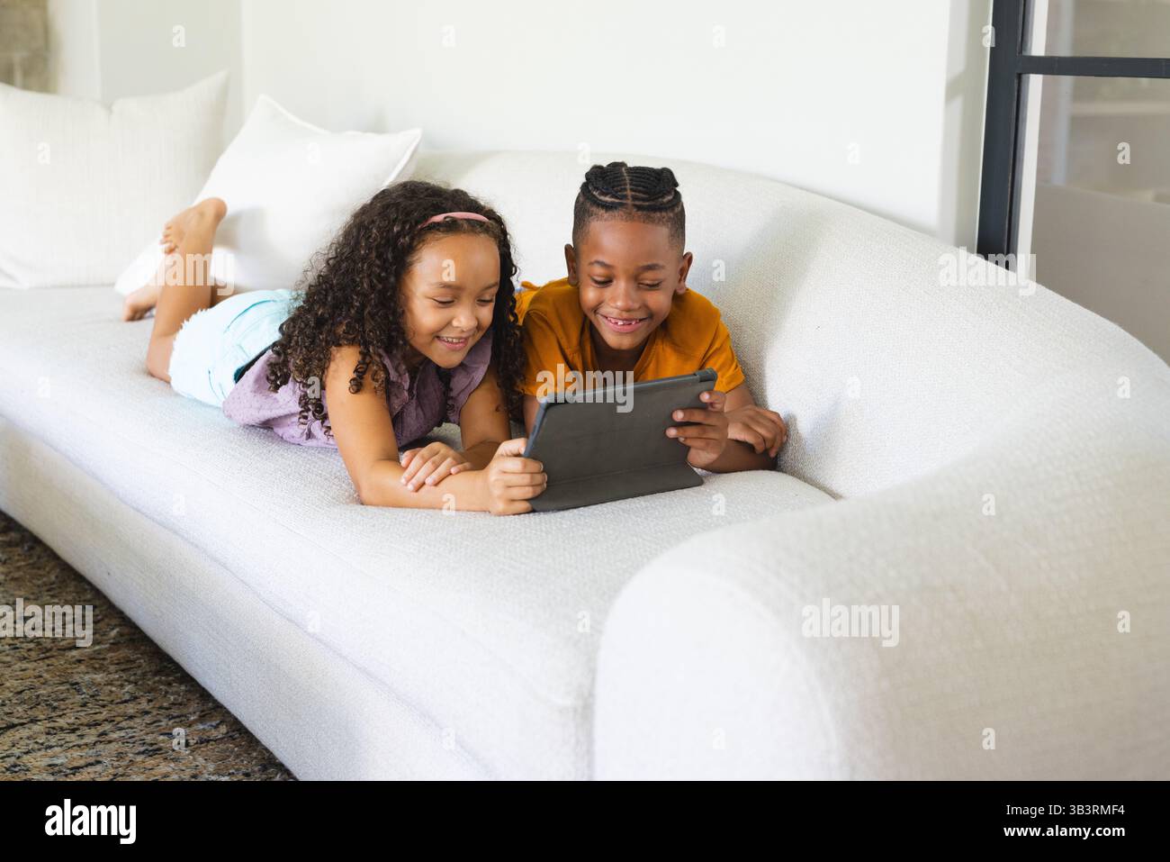 Lying Diverse siblings smiling on light-colored sofa in modern living ...