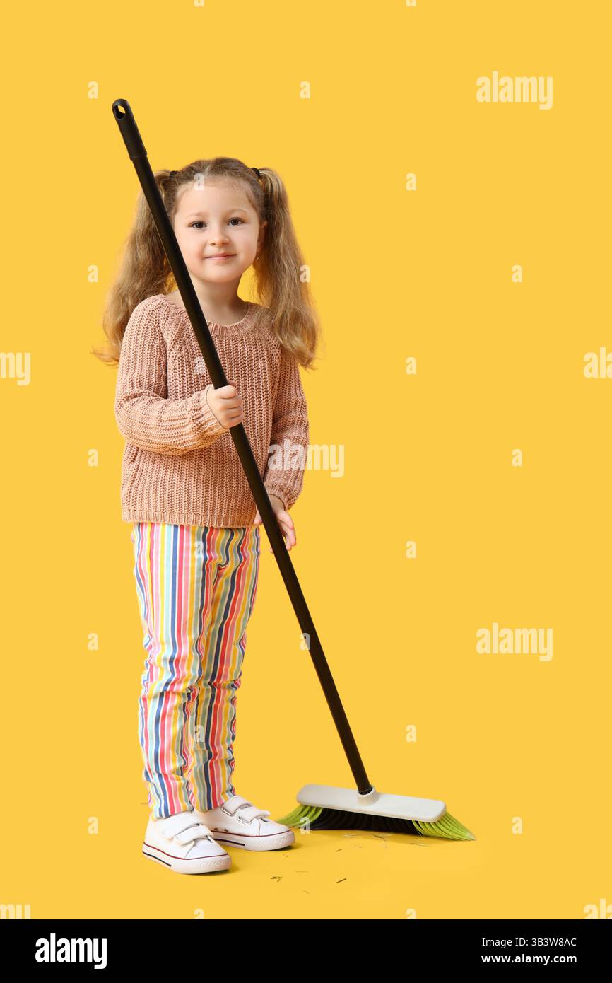 Cute little girl sweeping with broom on yellow background Stock Photo ...