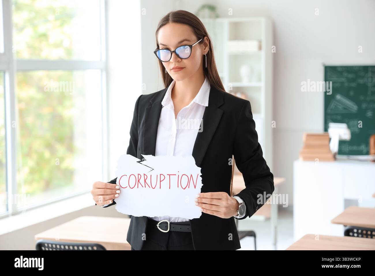 Female teacher holding paper with word CORRUPTION in classroom Stock ...