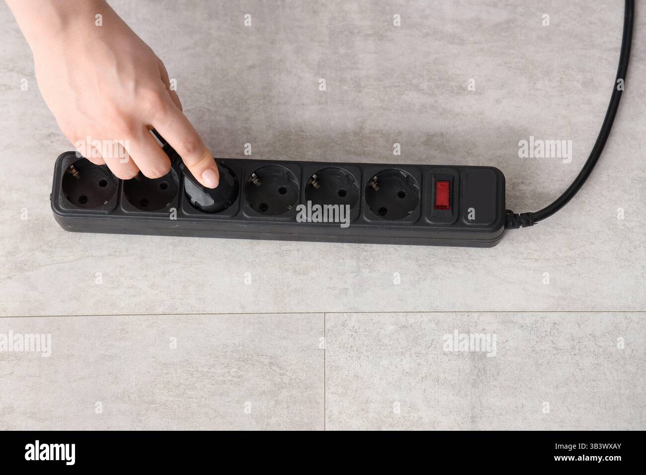 Female hand getting out plug from extension cord on floor, top view ...