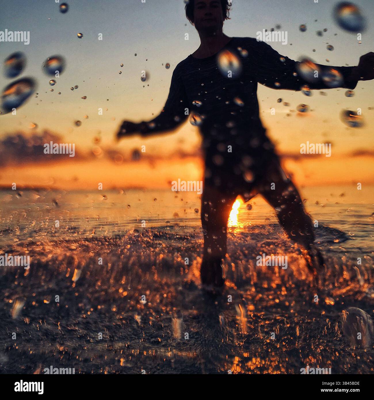Unrecognisable mans silhouette running on the sea and splashing water ...