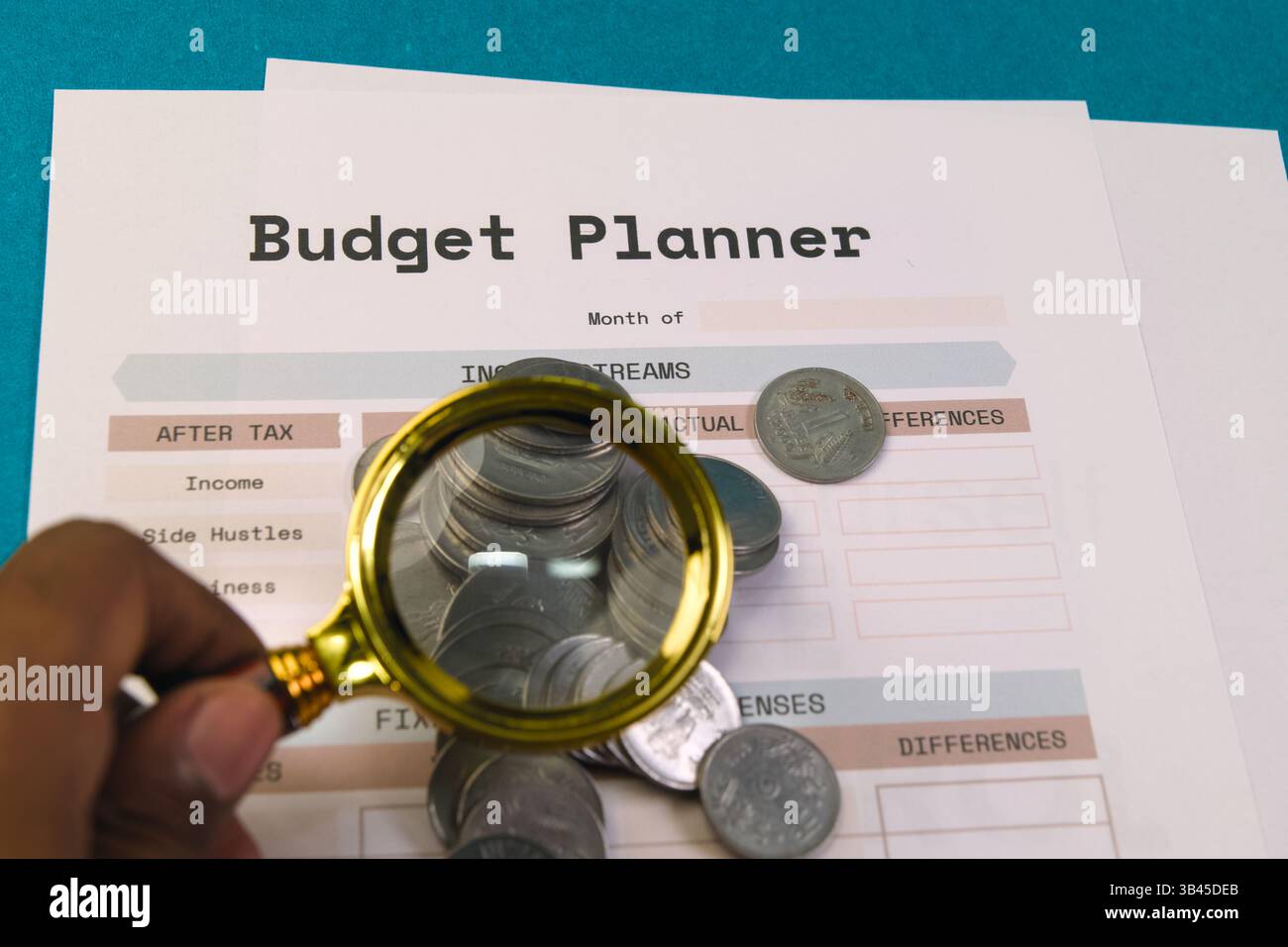 Hand holding a magnifying glass over coins and a budget planner ...
