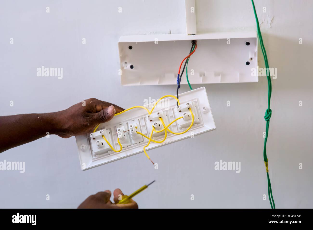 Skilled electrician works on wiring a new power outlet on a white wall ...