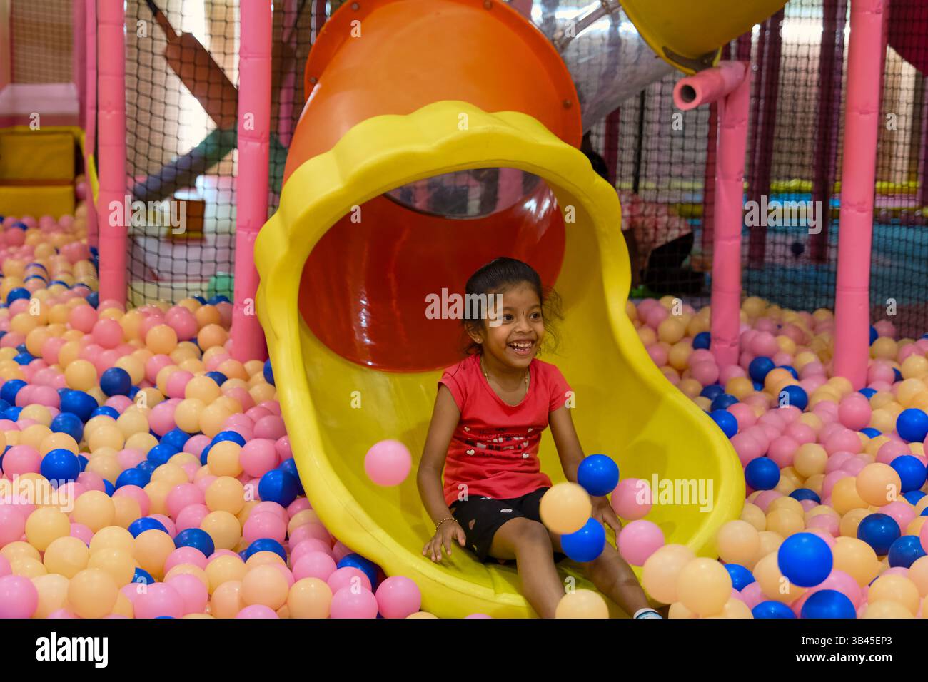 Child enjoys sliding down a yellow slide in a colorful indoor play ...
