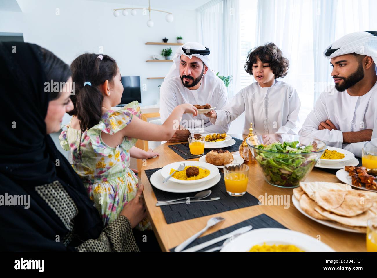 Happy arab family wearing emirati clothing spending time together at home during dinner after ...