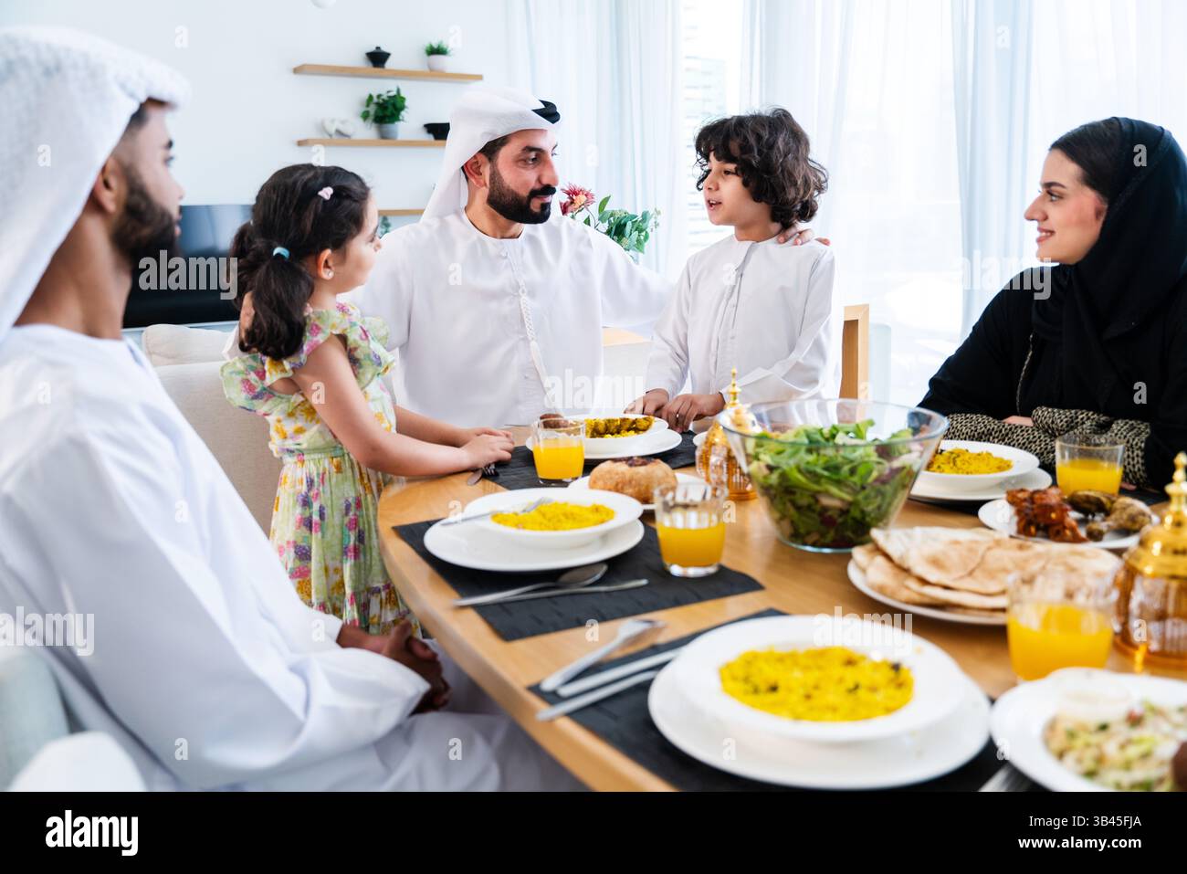 Happy arab family wearing emirati clothing spending time together at home during dinner after ...