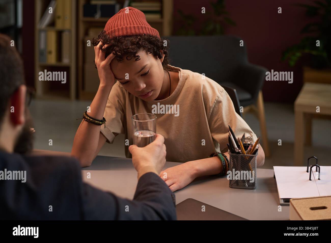Hand of professional school psychologist passing glass of water to sad ...