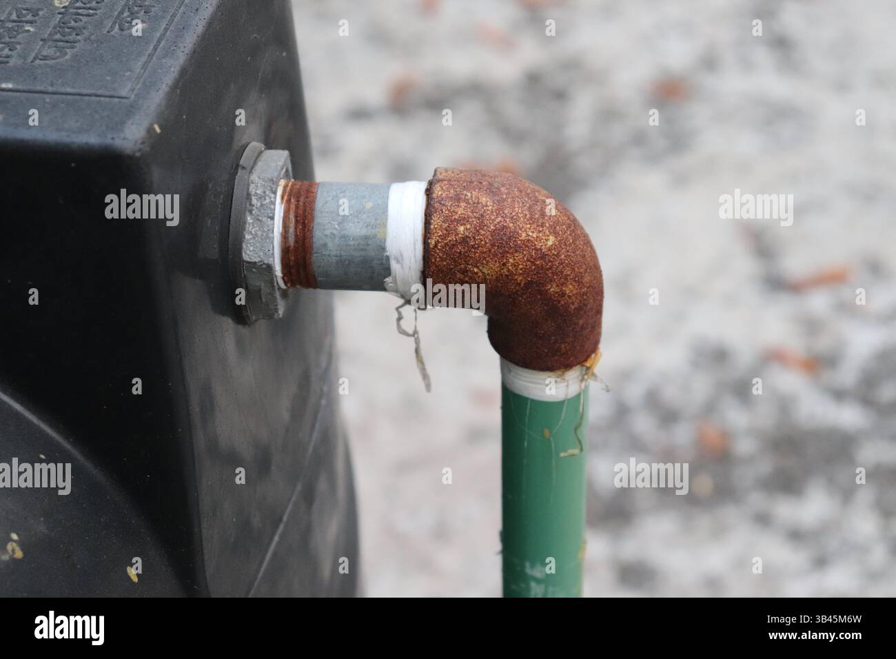 Close-up captures a corroded metal pipe fixed to a black plastic tank ...