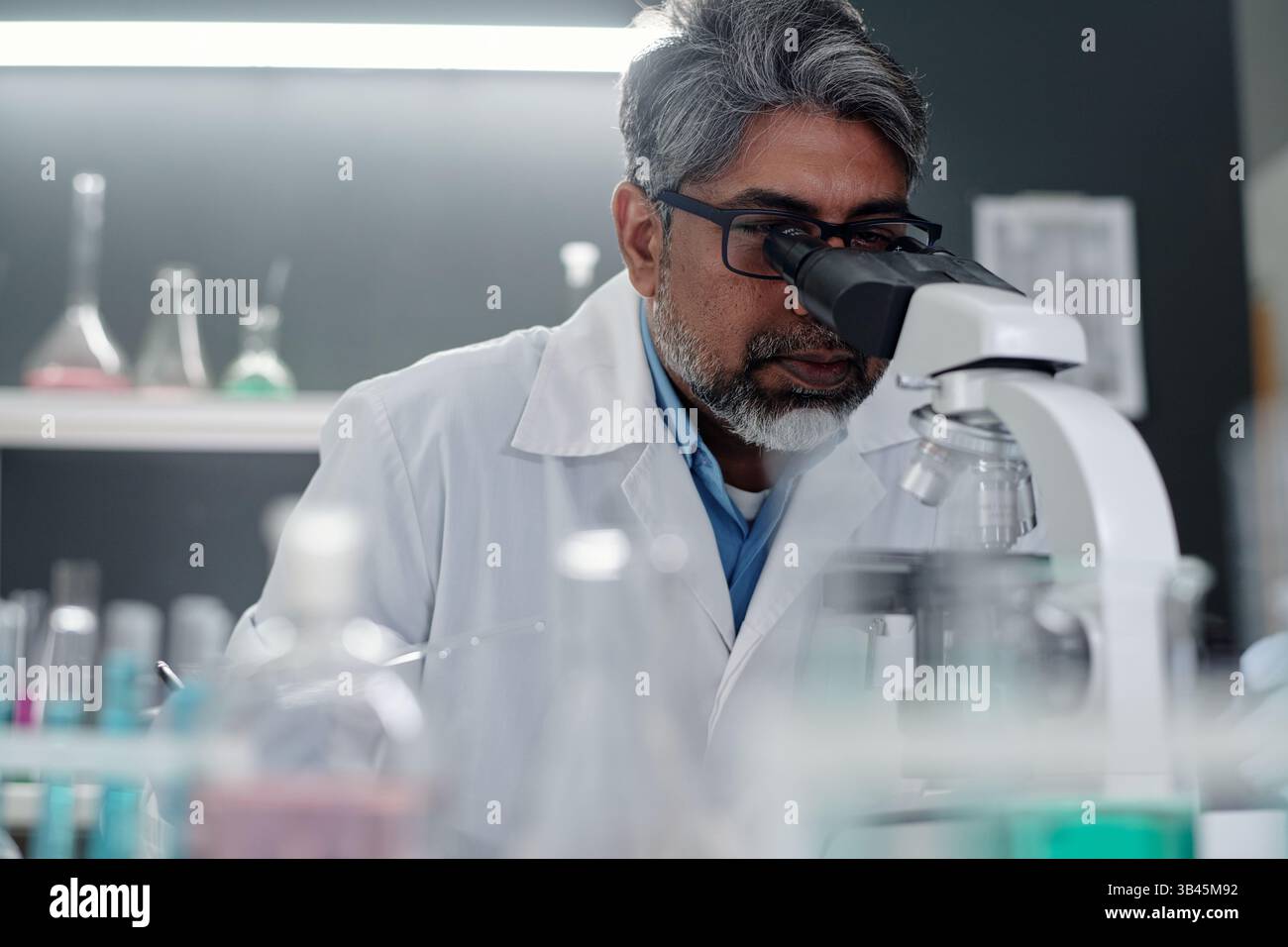 Middle-aged scientist examining samples under microscope in laboratory ...