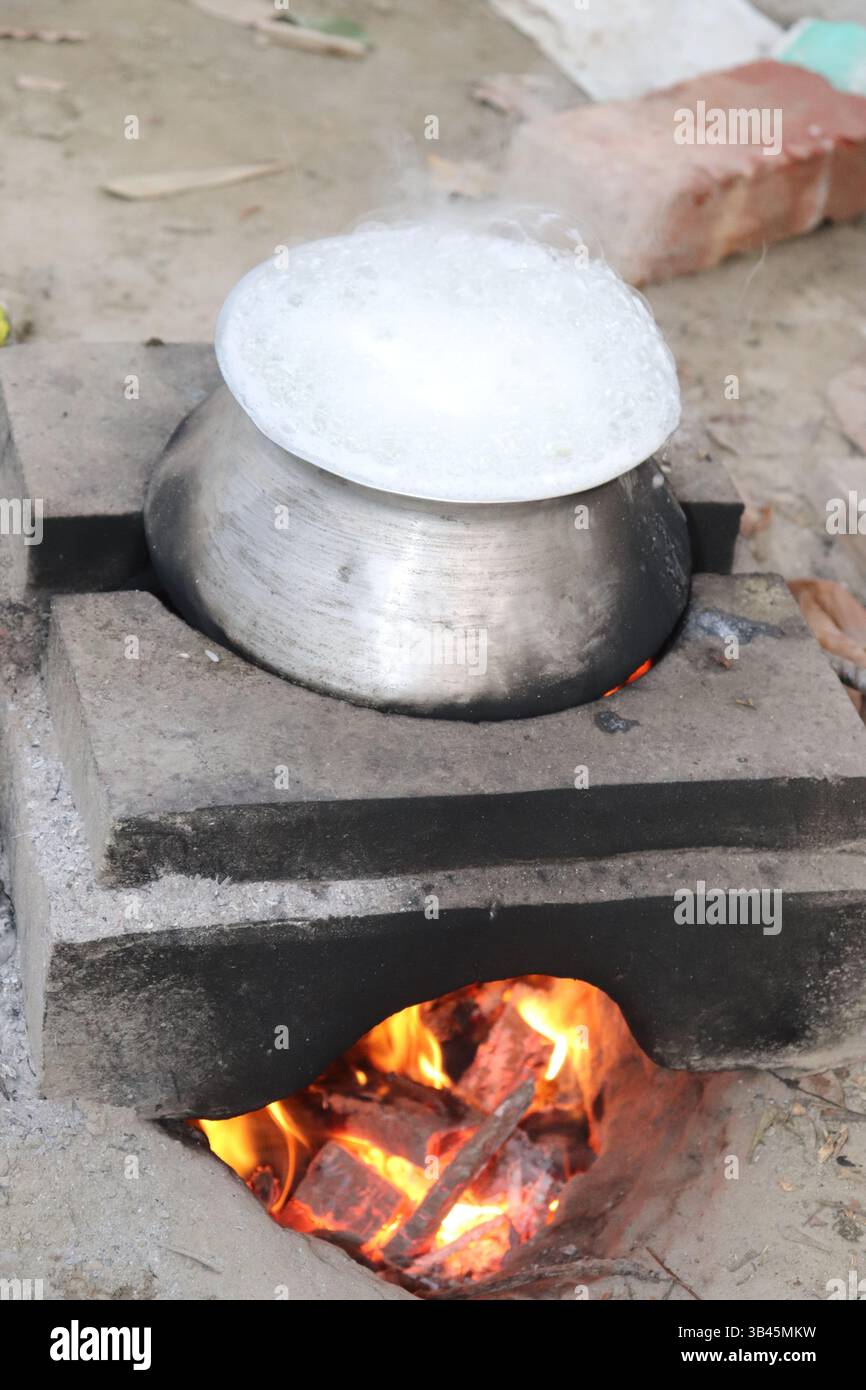 View of silver pot boiling over on a brick stove with fire and wood ...