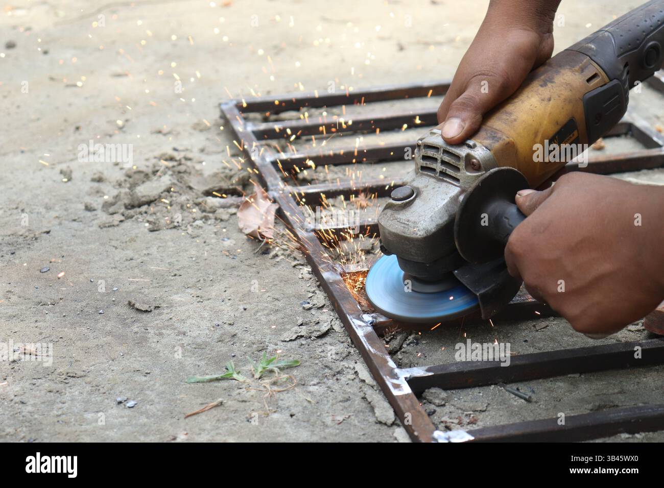 Dark-skinned craftsman smoothing brown metal frame using power tool in ...