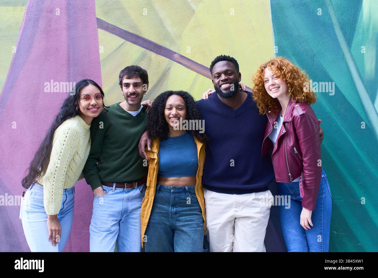 Five cheerful young friends are posing together with arms around each ...
