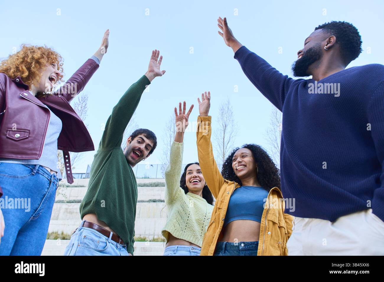 Five multi ethnic young adults giving high five with their hands raised ...
