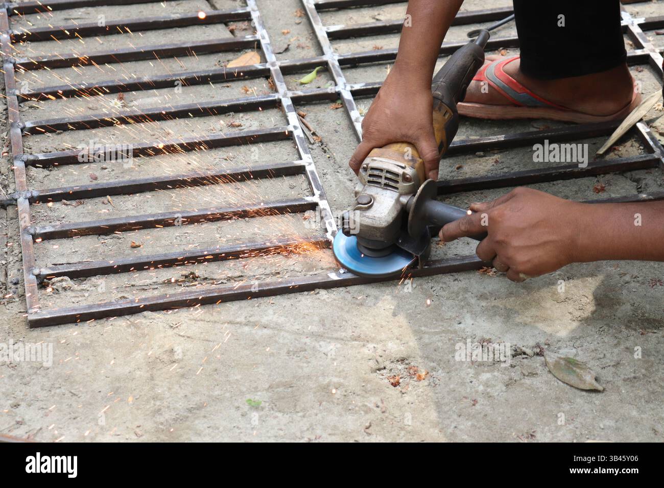 Close up shot featuring an Asian man grinding metal with a hand tool ...