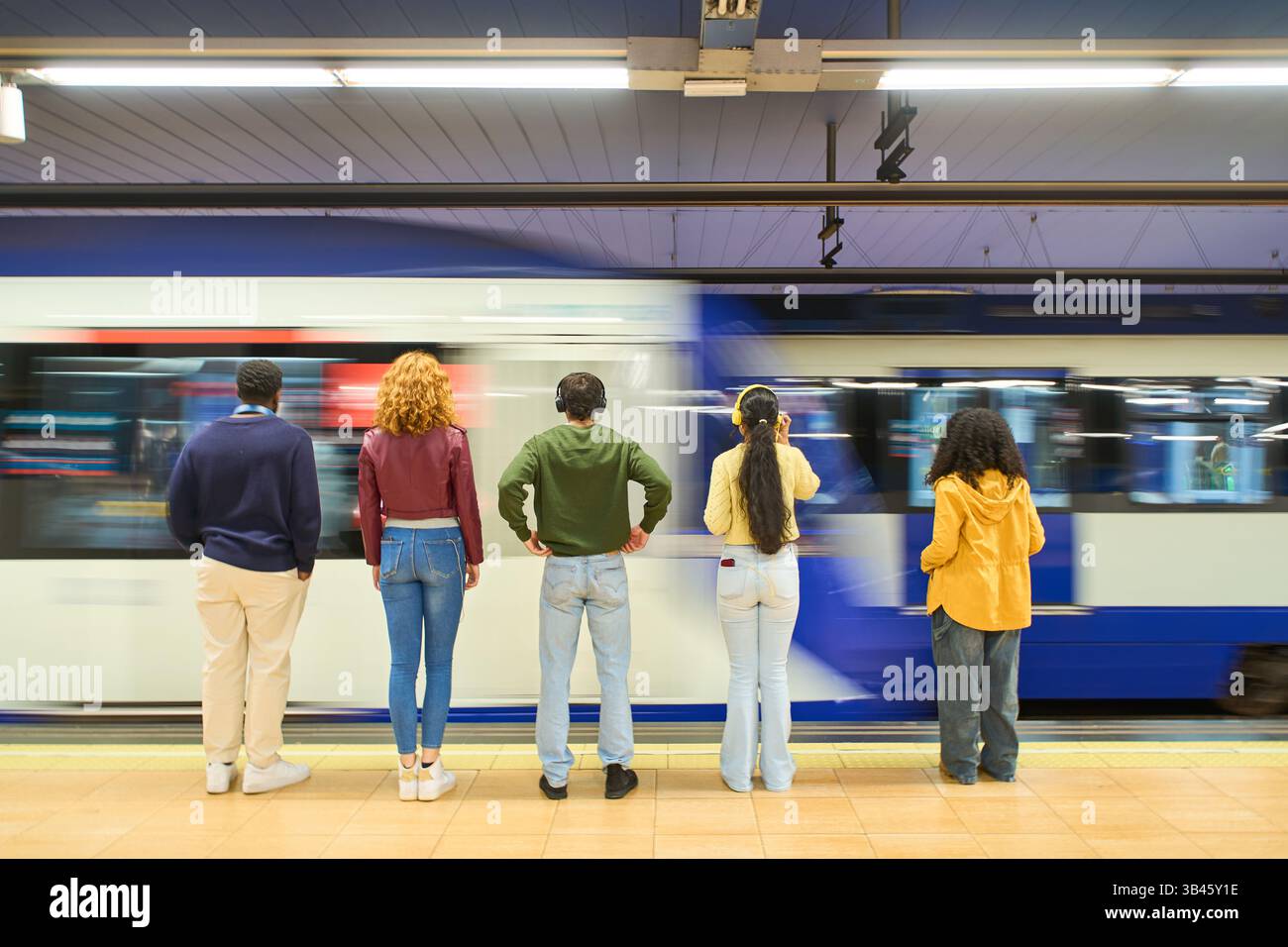 Five young students waiting for an arriving train at a bustling subway ...