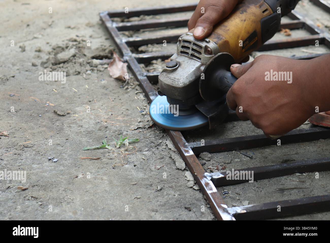 Dark-skinned worker uses an angle grinder to refine metalwork. The ...