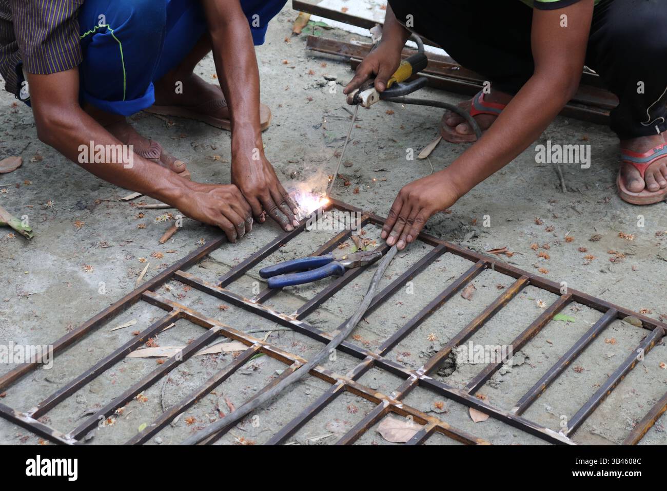 Close-up shot focusing on two Asian men welding a metal grid on ground ...