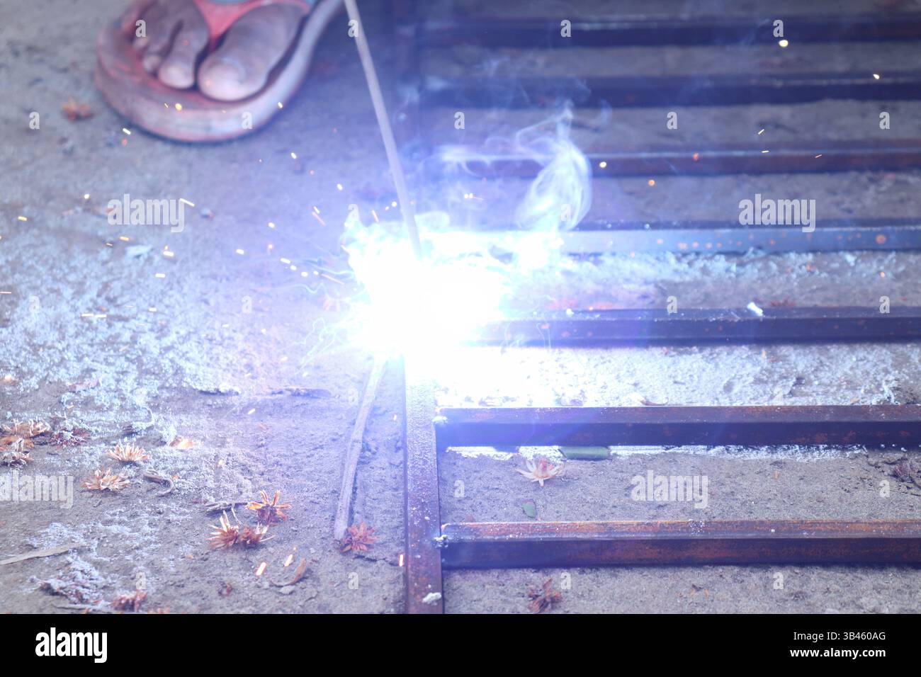 An unidentified person is welding a metal fence, producing intense ...