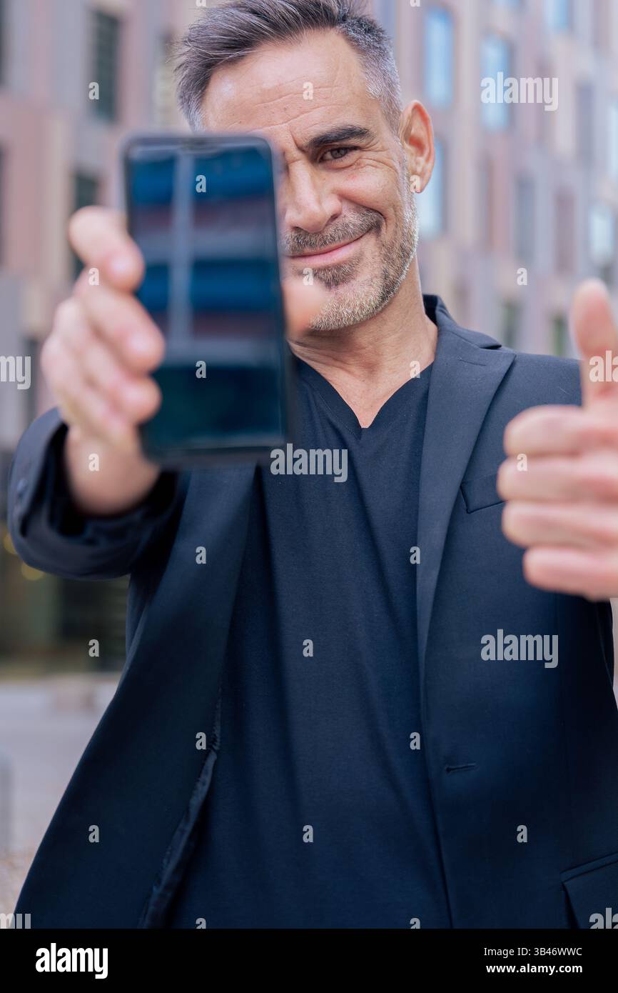 Man holding smartphone towards camera and showing thumbs up in outdoor ...