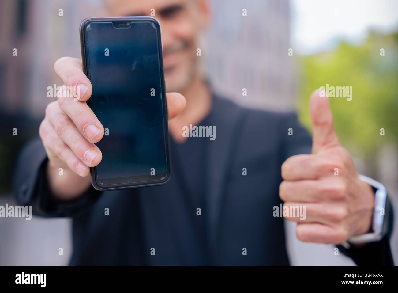 Man holding smartphone towards camera and showing thumbs up in outdoor ...