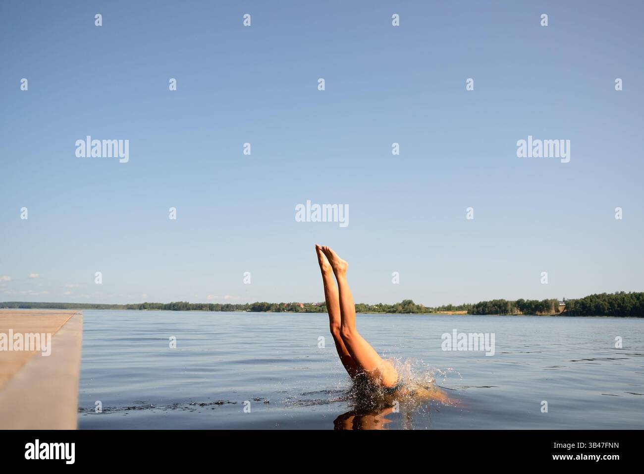 Woman in a swimsuit jumping headfirst from a pier into a lake ...