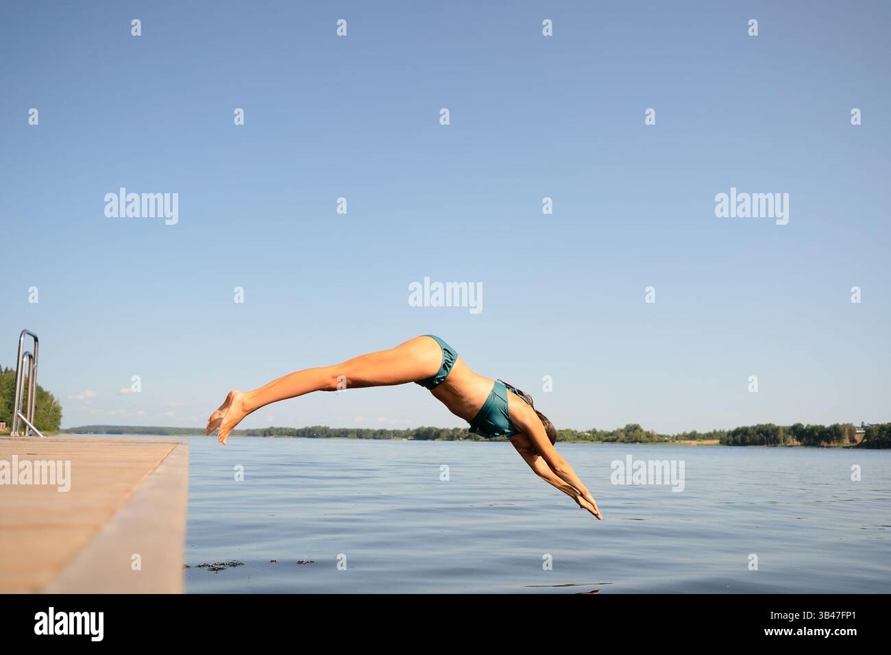 Athletic woman in swimsuit diving headfirst from a pier into the lake ...
