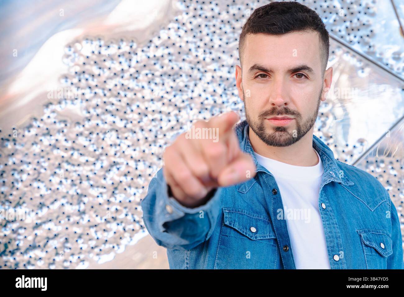 Serious man pointing at camera with focus gesture and abstract ...