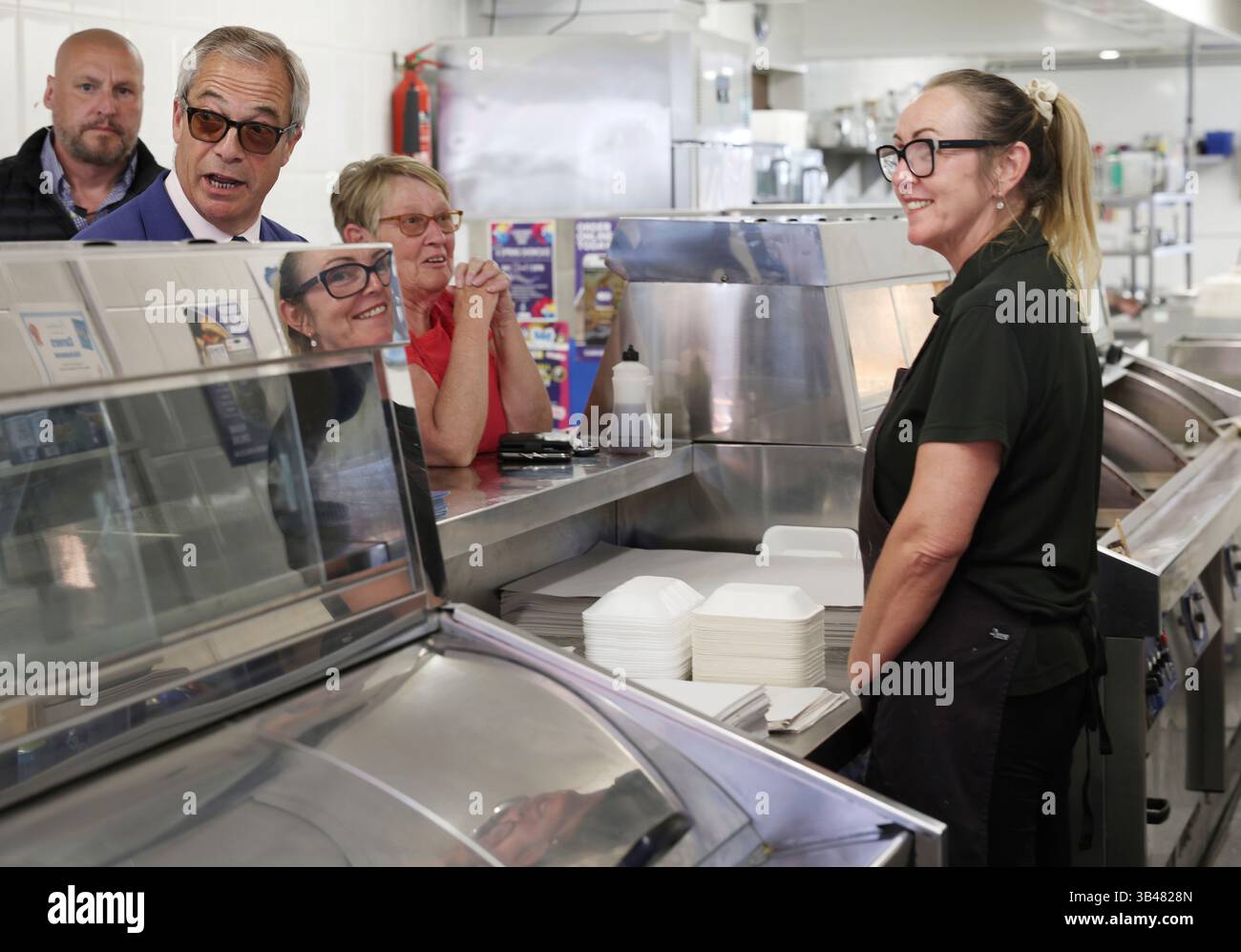 Reform UK leader Nigel Farage speaks to a woman behind the counter of a ...