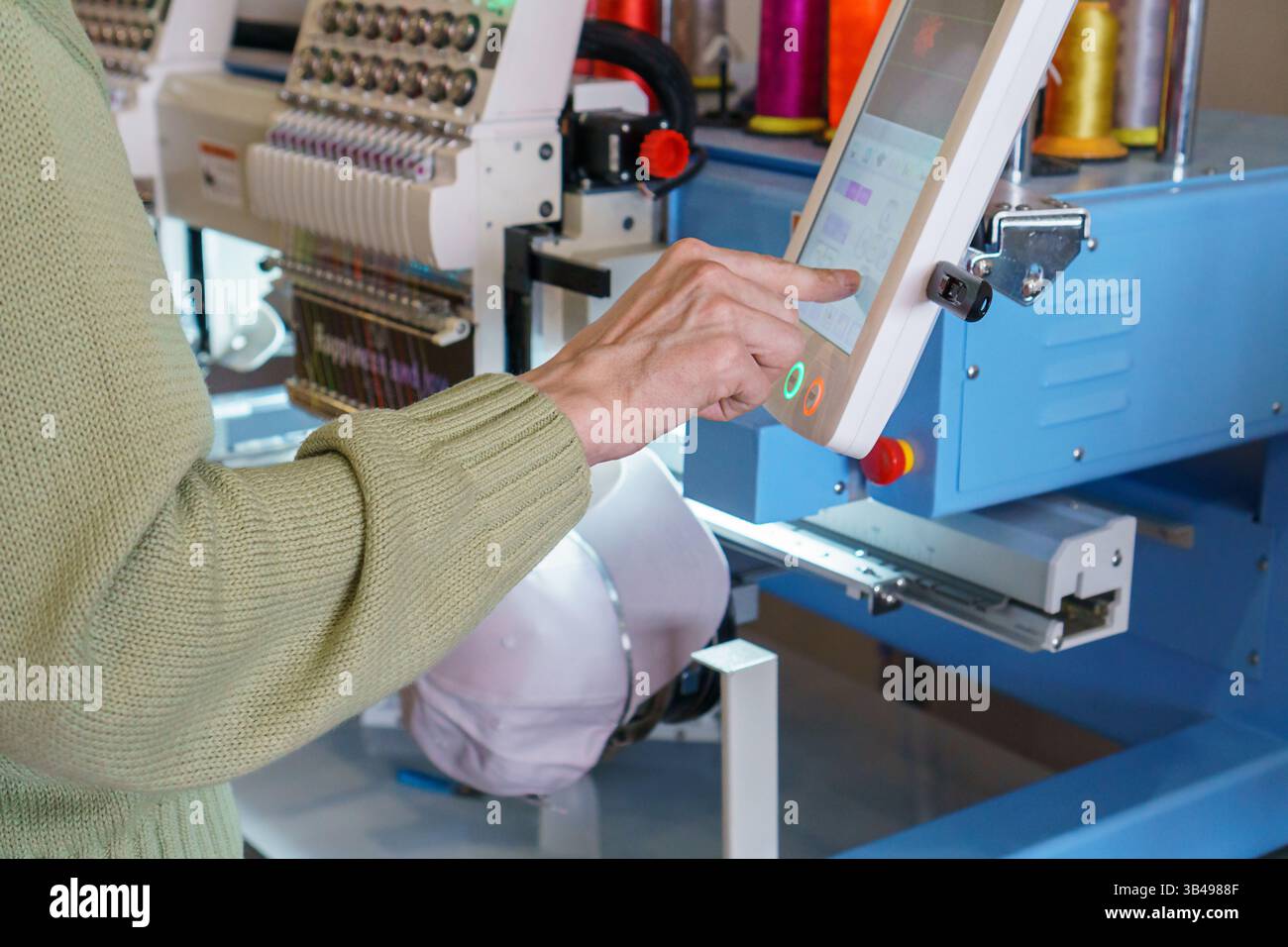 Man's hand pointing onthe screen of embroidery machines next to ...