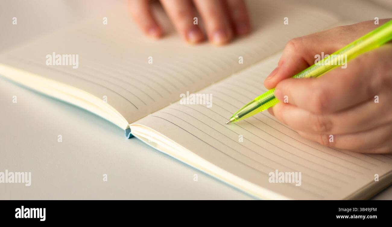 Left handed person making notes on blank page on notebook during ...