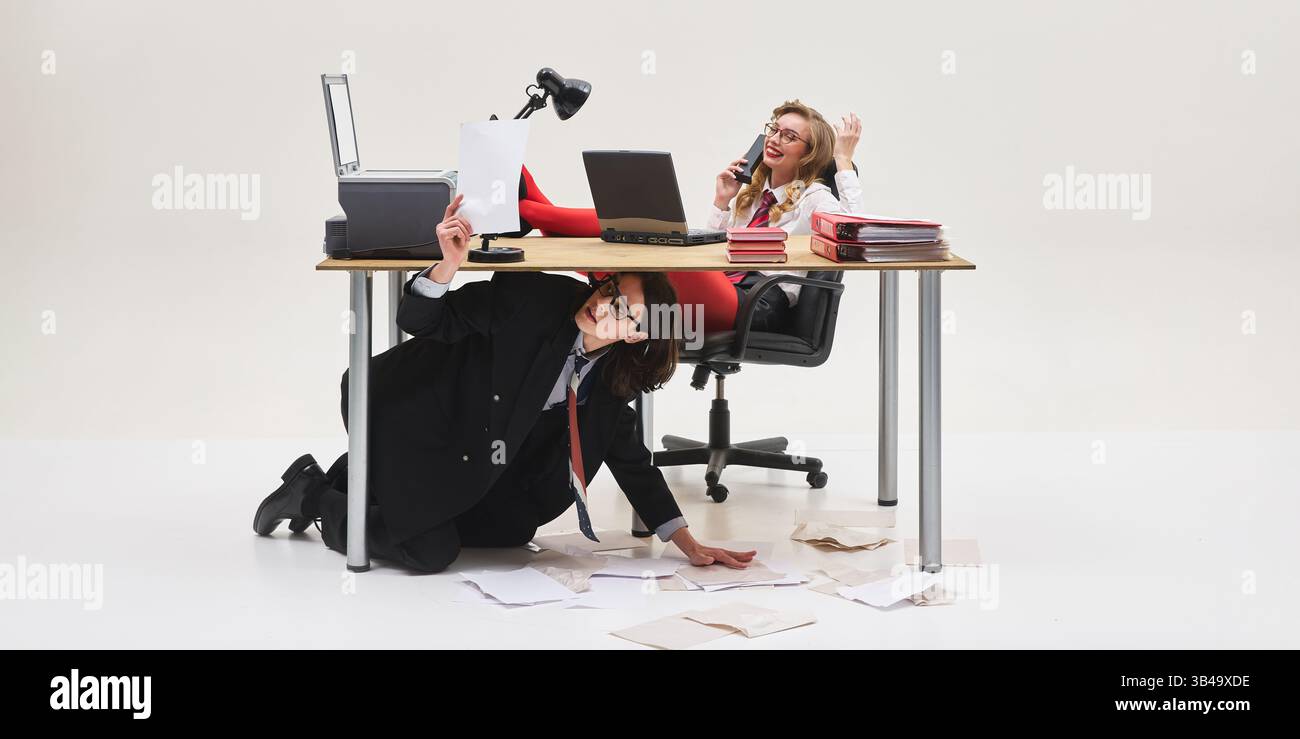 Female worker laughing on phone with legs on desk while male colleague ...