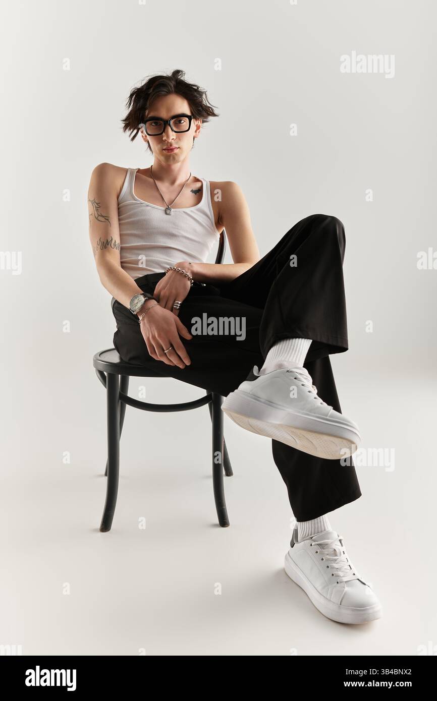A slim young man poses confidently in a white tank top and trendy ...