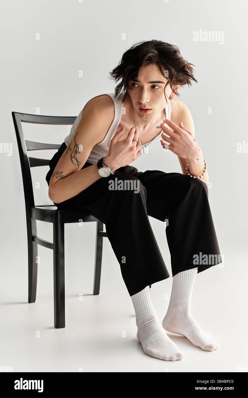 Slim young man seated on a chair expresses a trendsetting look with ...