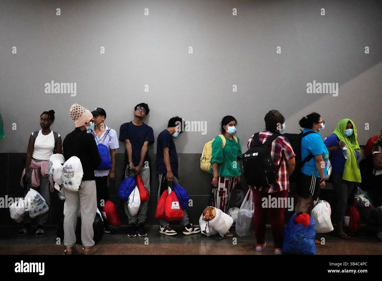 Migrants, mostly from Asian countries, wait for transport to hotels ...