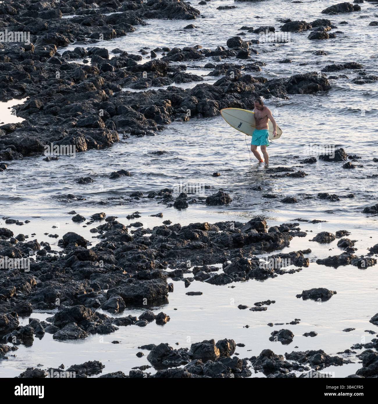 View of a man holding a surf board walking out of the ocean towards the ...