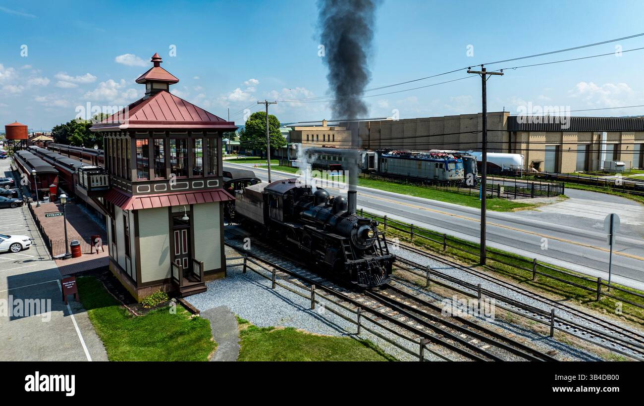 A classic steam train releases smoke as it pulls away from an old-style ...
