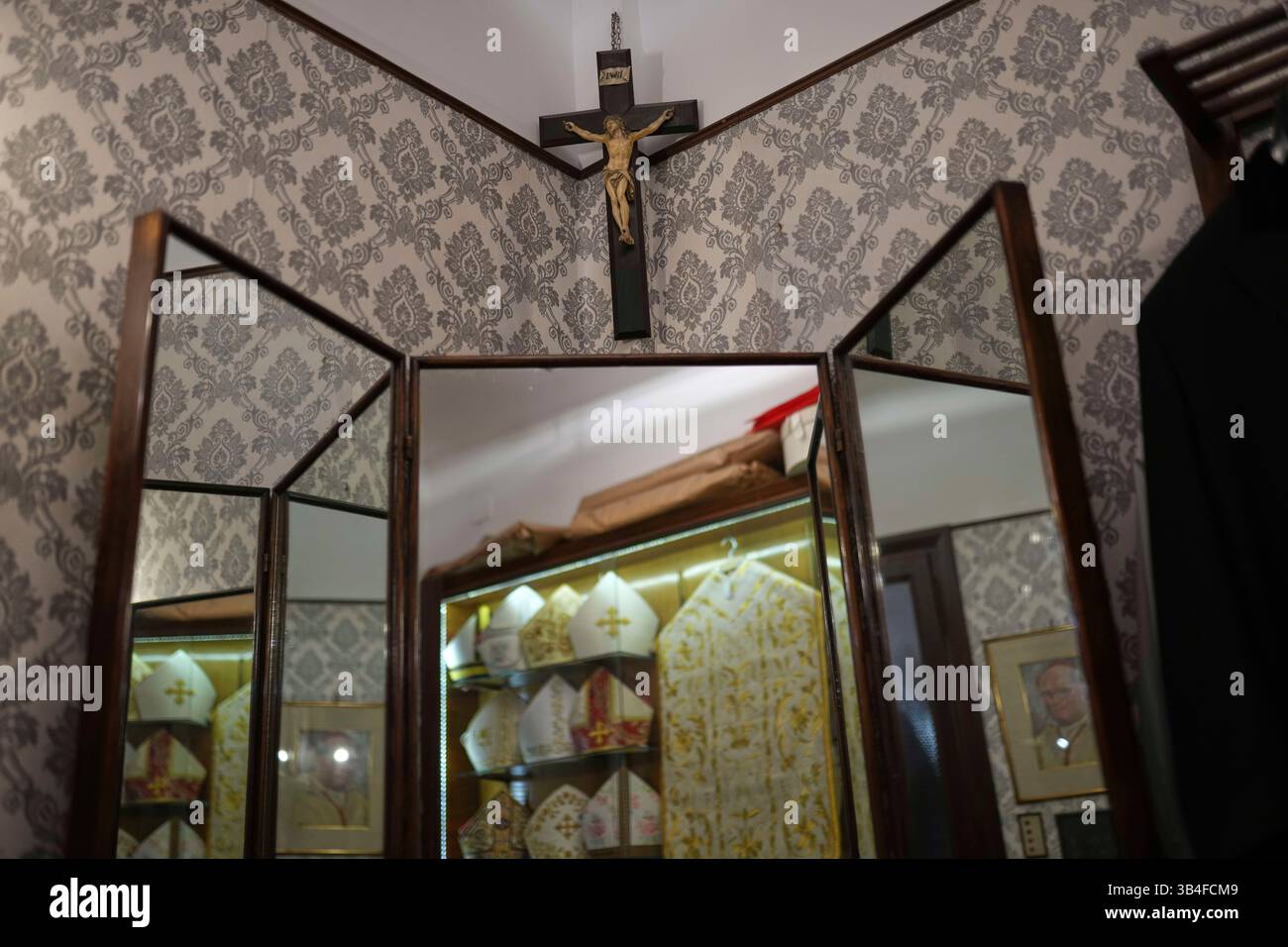 A crucifix hangs over a mirror reflecting ecclesiastic clothes inside ...