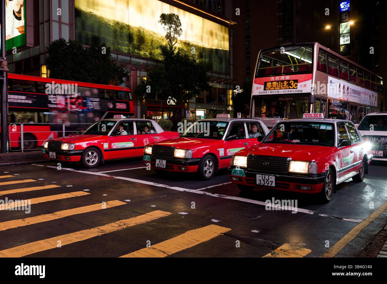 Iconic red taxis pause at a crosswalk as a double-decker bus rushes ...