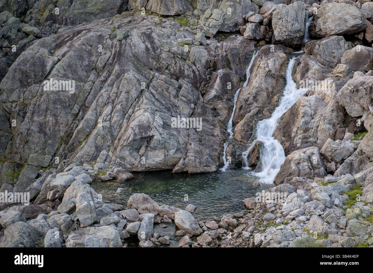 Small cascading waterfall flowing through rugged rock formations into a ...
