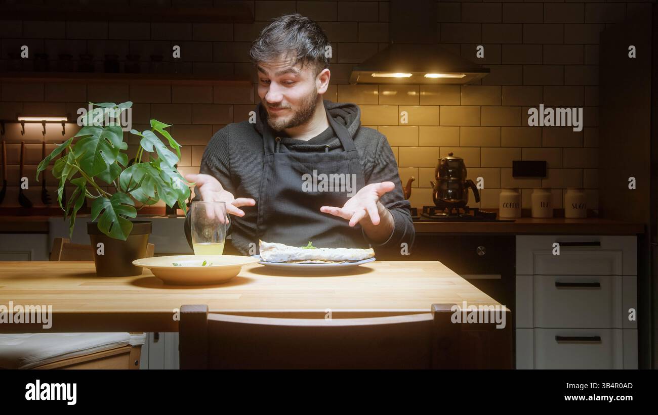 Satisfied man enjoying late night snack at kitchen table giving thumbs ...